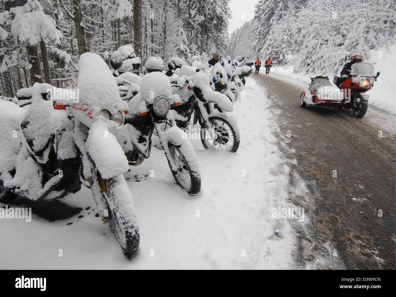 Motorcycles covered in snow stand at the side of a road at the so ...