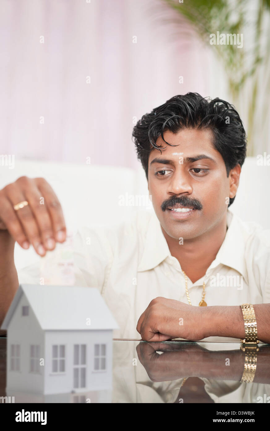 South Indian man putting money in a model home Stock Photo - Alamy
