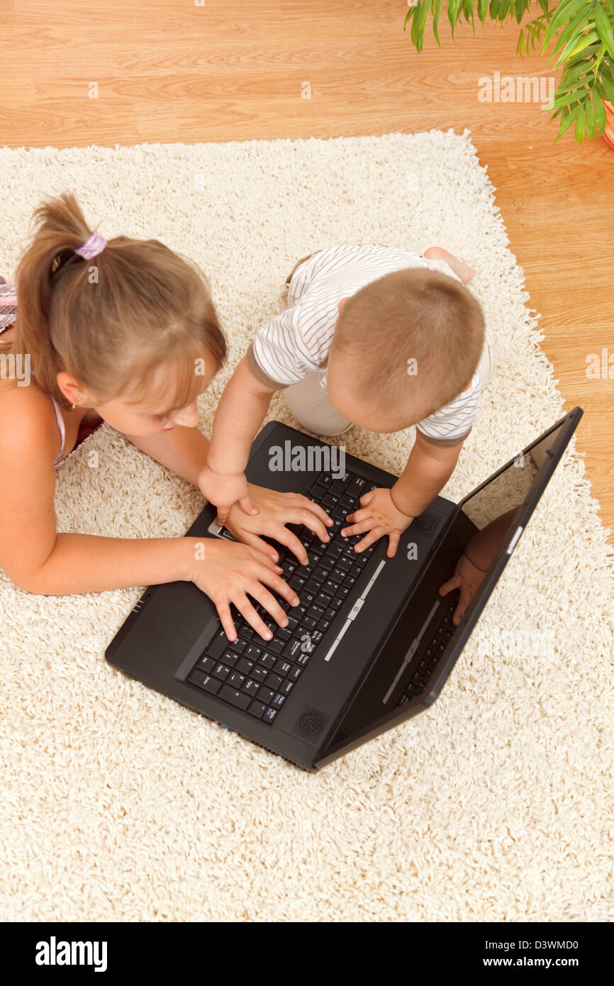 Top view of a girl typing on laptop while her brother is disturbing ...