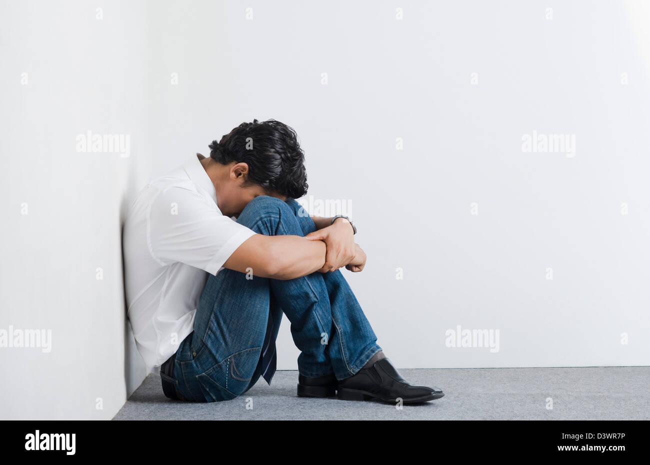 University student sitting in the corner with head down Stock Photo - Alamy