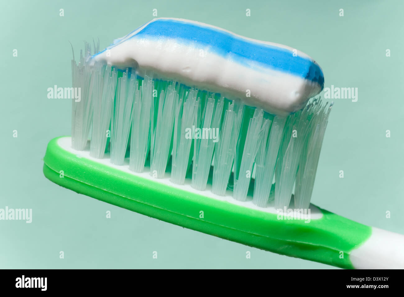 close up view of toothbrush and some toothpaste on it on green back ...