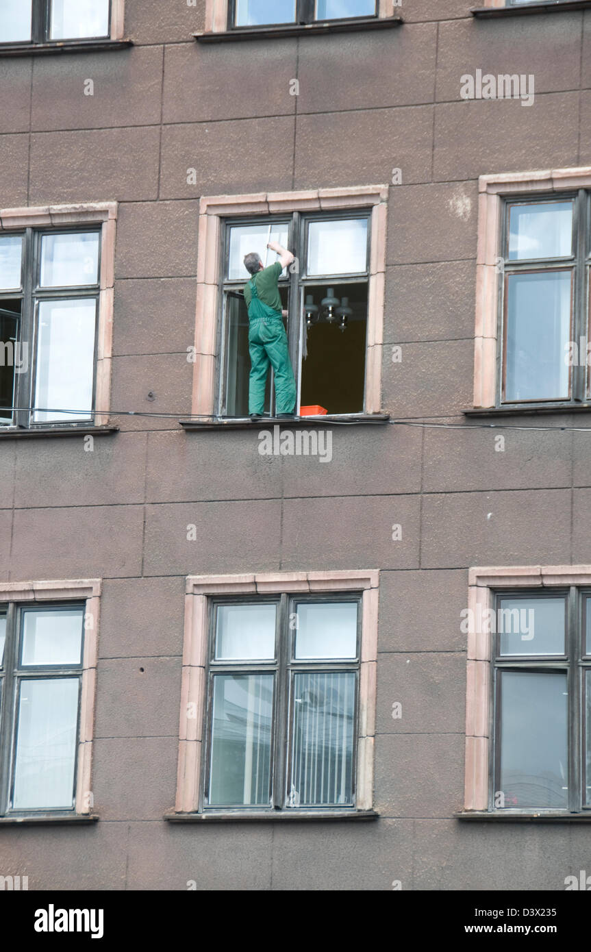 A window cleaner standing on the window ledge of a tall office building ...