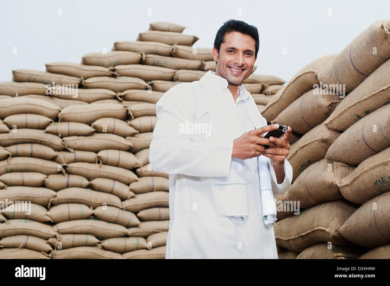 Man standing near stacks of wheat sack holding a mobile phone, Anaj ...