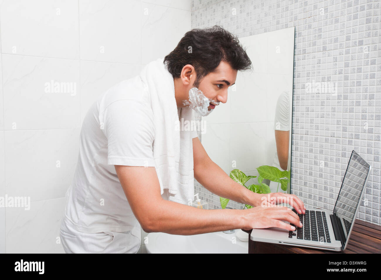 Man using a laptop while shaving his face Stock Photo - Alamy