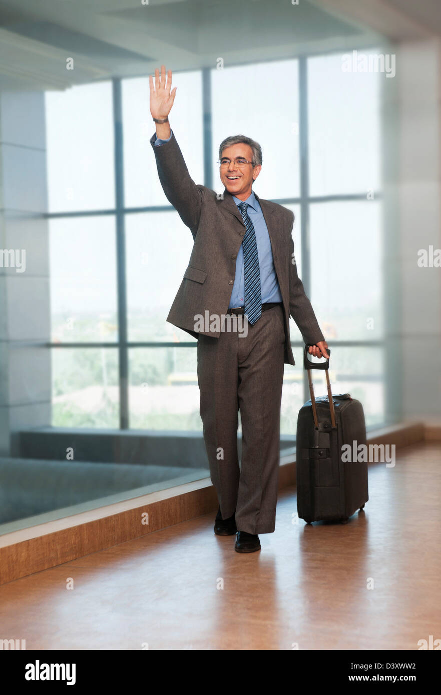 Businessman pulling a trolley bag and smiling Stock Photo - Alamy
