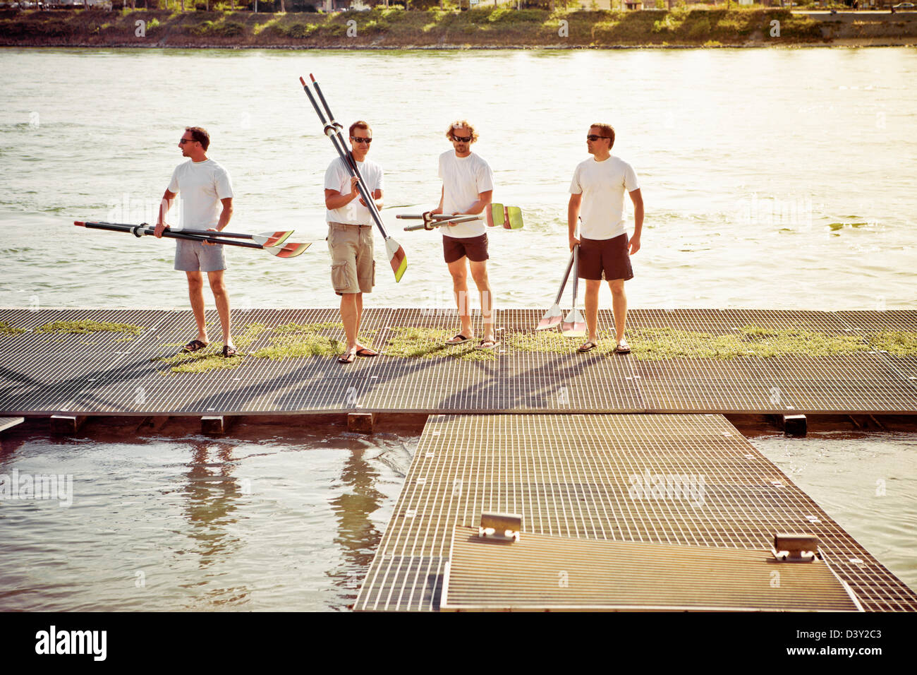 Male rowing team carrying paddles on shoulders coming in after a rowing ...