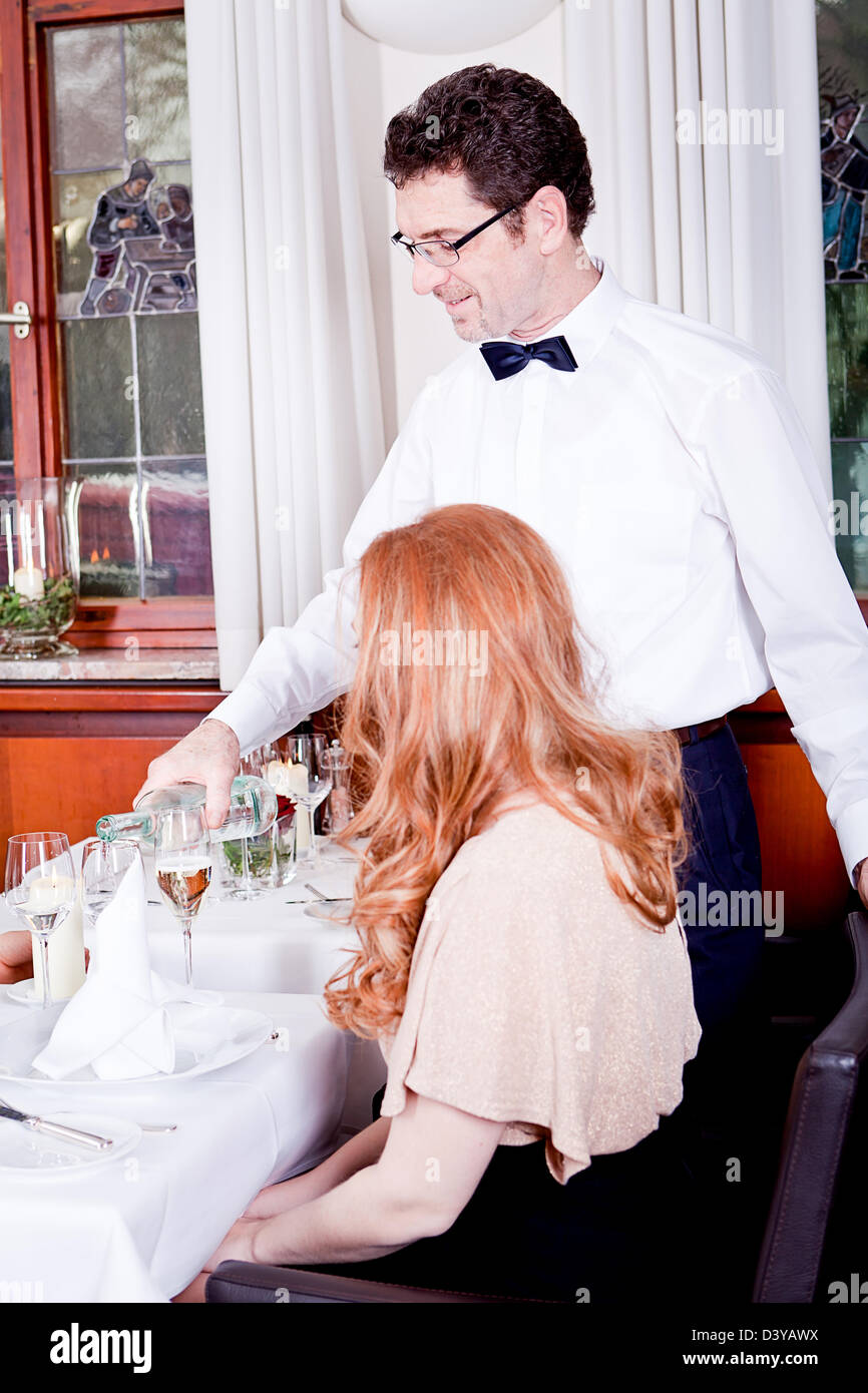 man and woman for dinner in restaurant waiter serving mineral water ...