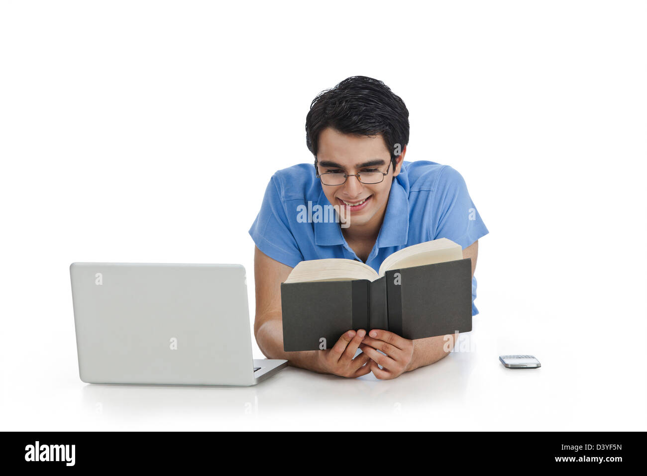 Happy man lying in front of a laptop and reading a book Stock Photo - Alamy