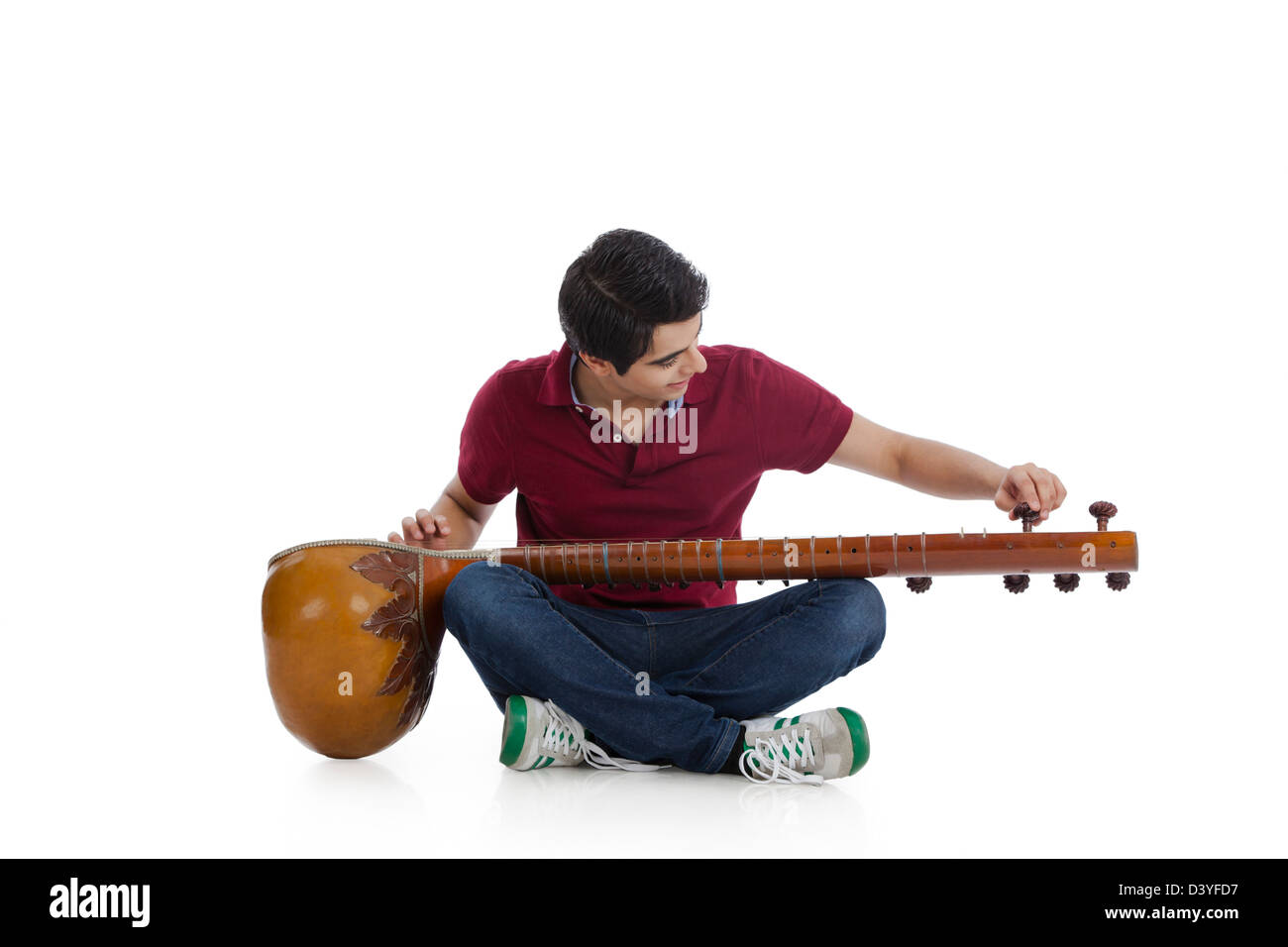 Man sitting on the floor and adjusting his sitar Stock Photo - Alamy