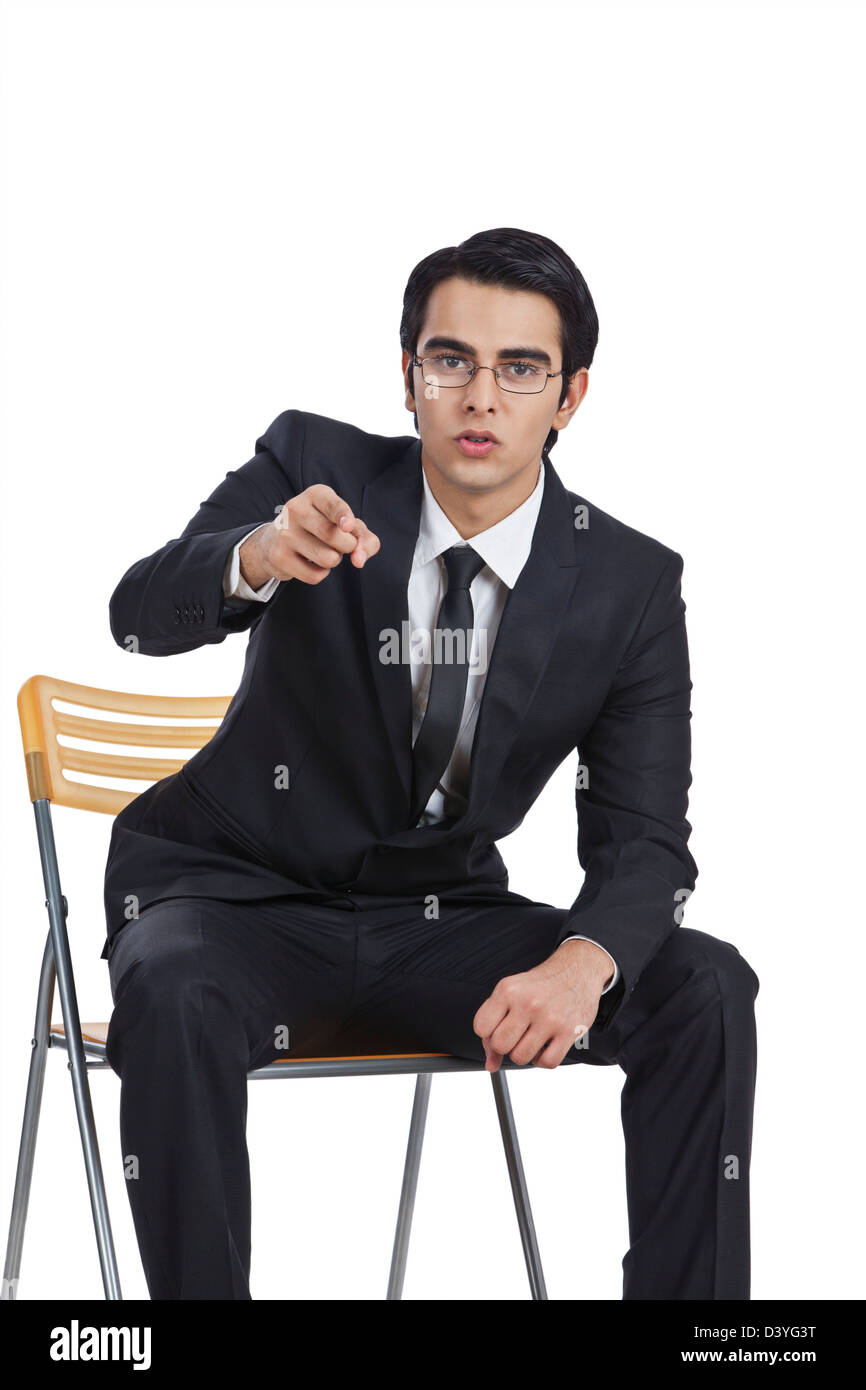 Portrait of a businessman sitting on a chair and pointing Stock Photo ...