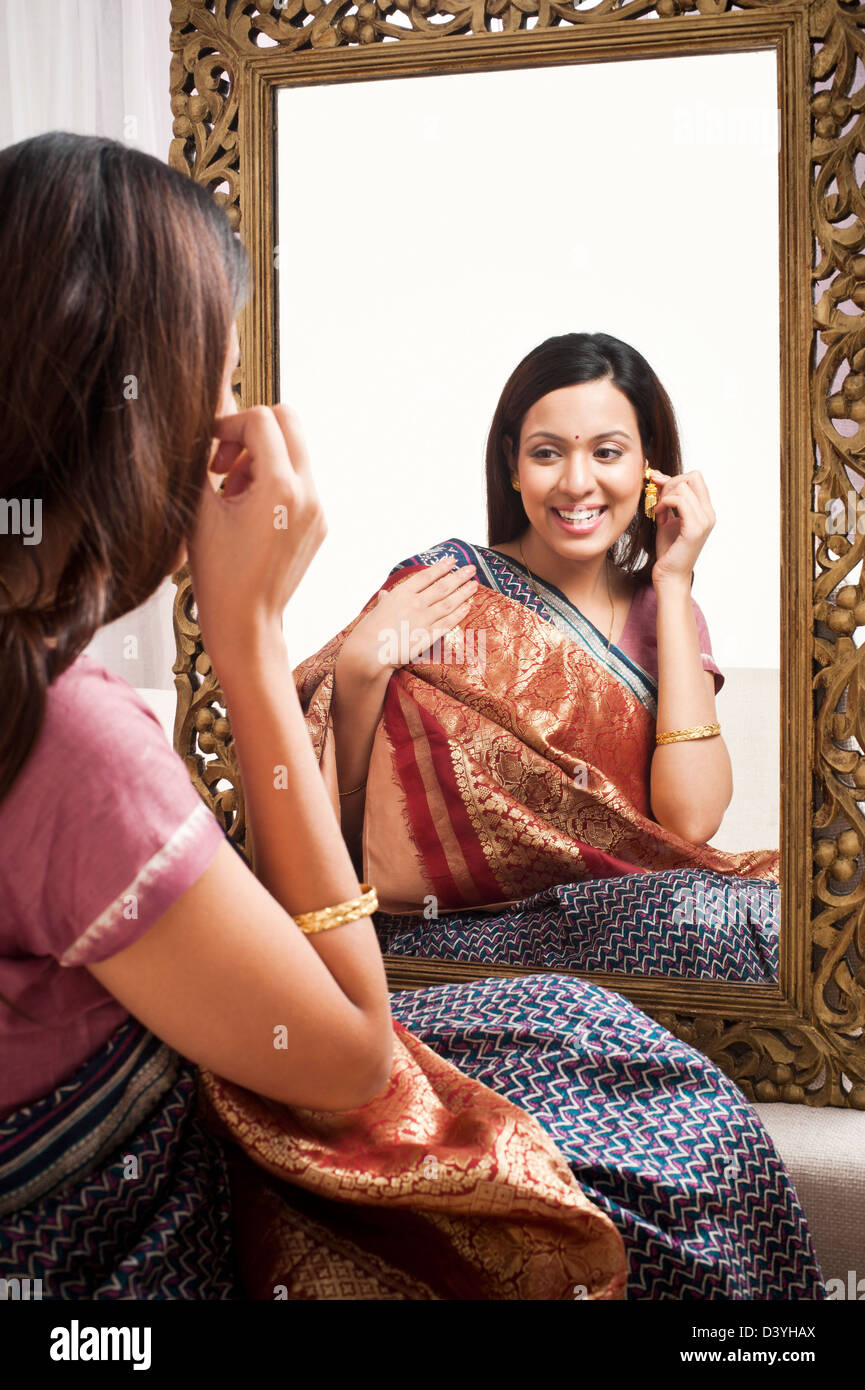 Reflection of a woman in mirror trying a sari and earring on herself ...