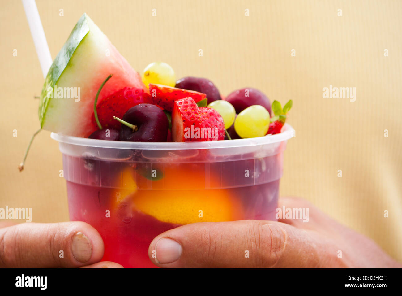 A man's hands hold a glass of pink lemonade overflowing with colorful ...