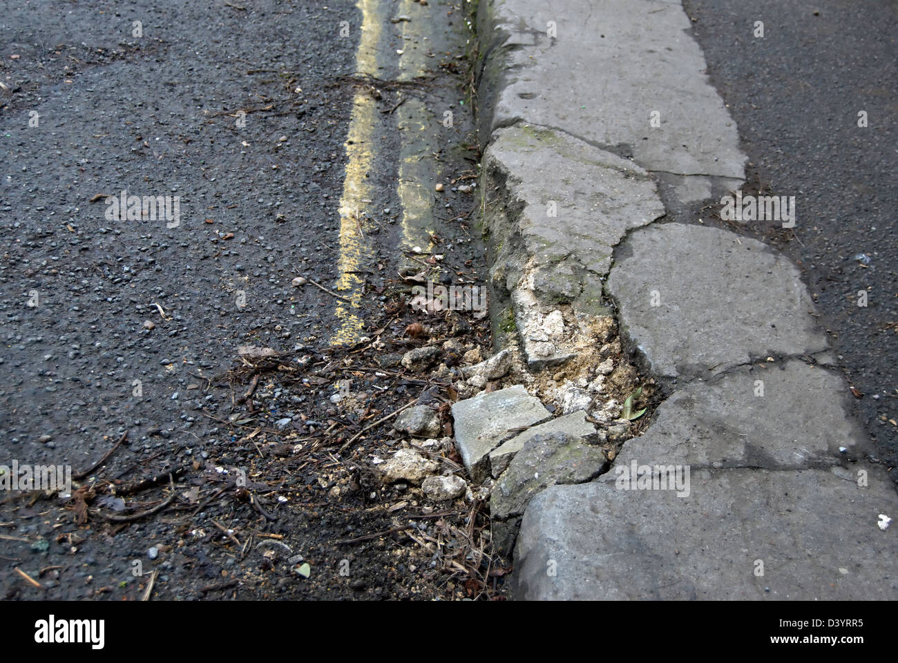 damaged kerb with rubble spilling over double yellow line road marking ...
