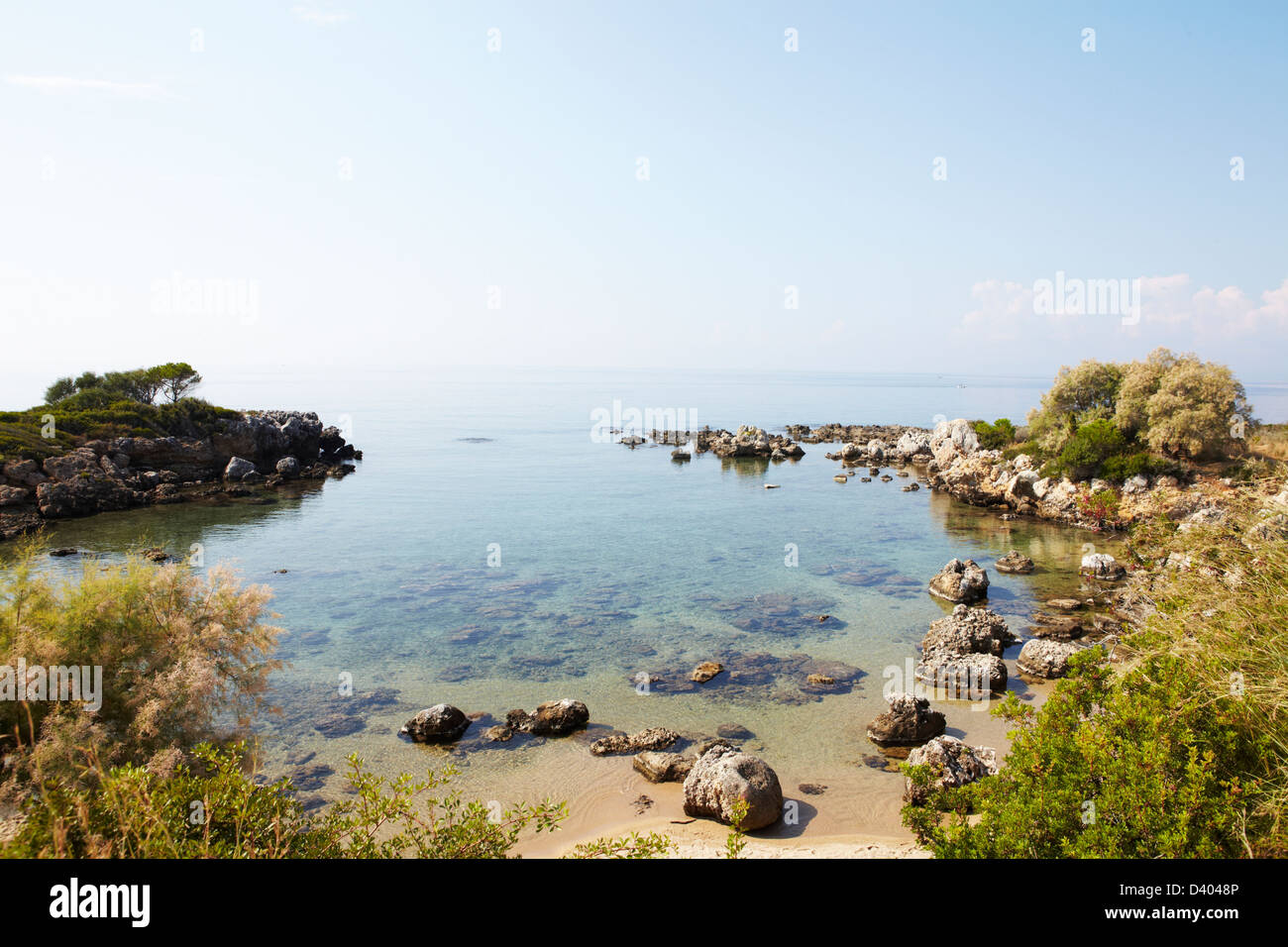A calm still view across a sheltered beach in Greece with large blue ...