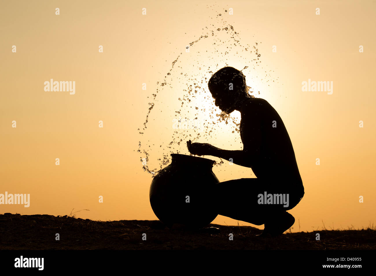 Indian man splashing water over himself from a water pot at sunset ...