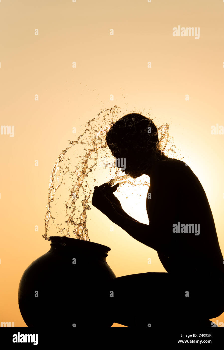 Indian man splashing water over himself from a water pot at sunset ...