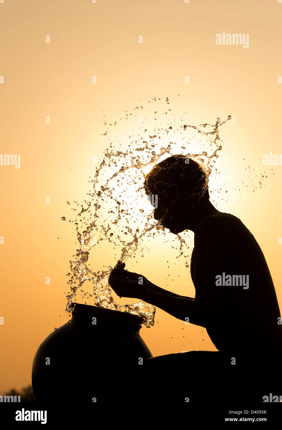 Indian man splashing water over himself from a water pot at sunset ...