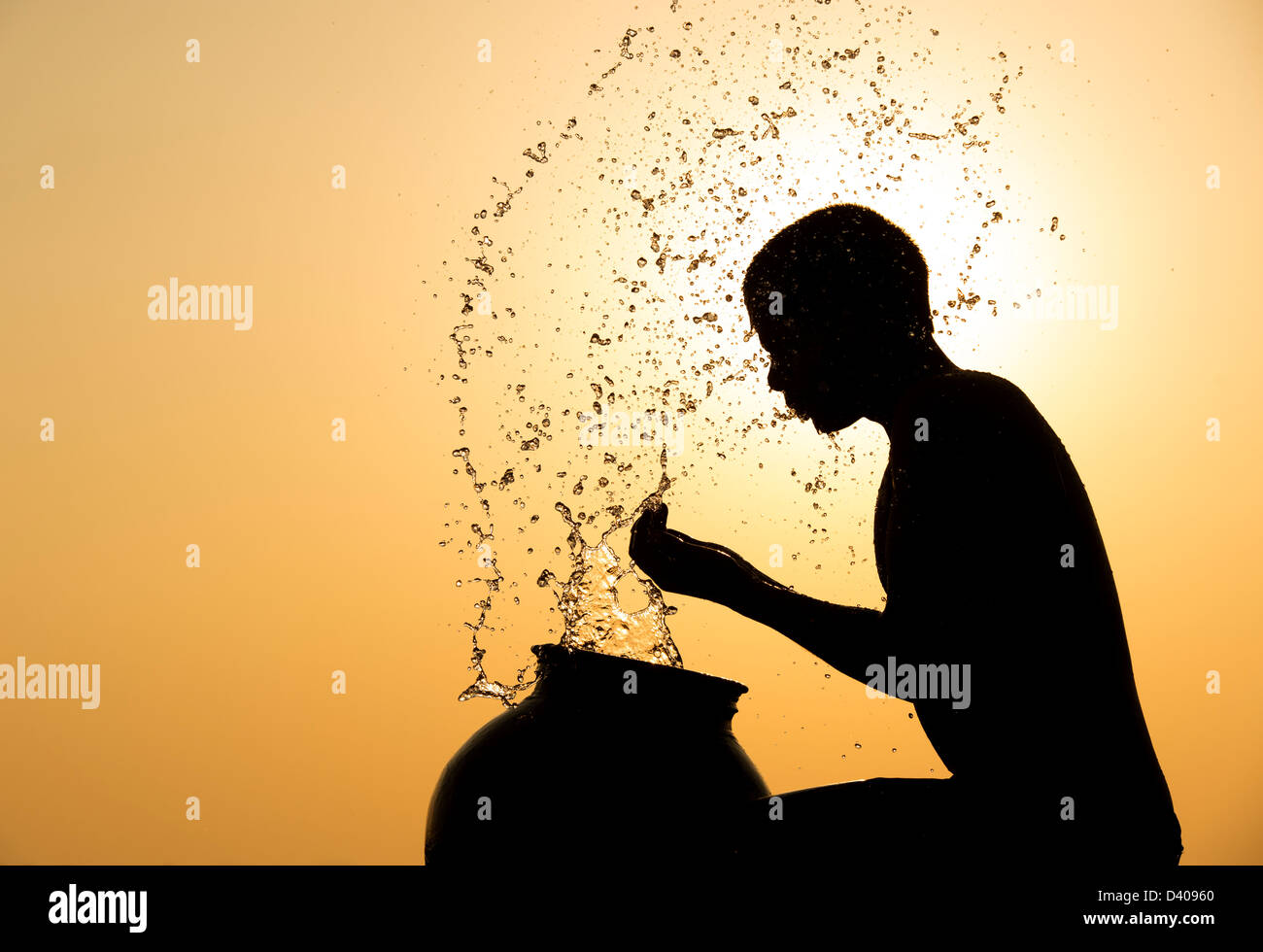 Indian man splashing water over himself from a water pot at sunset ...