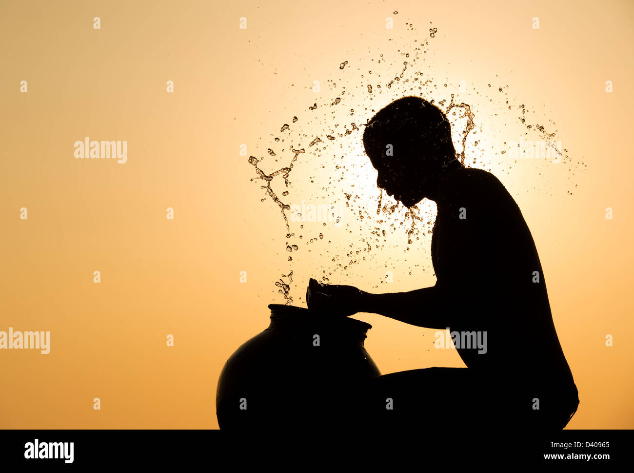Indian man splashing water over himself from a water pot at sunset ...