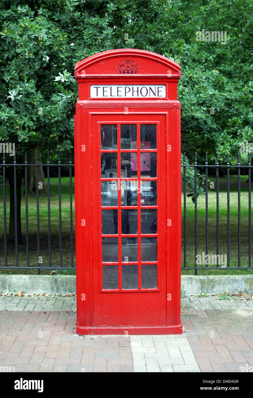 Red telephone box on brick paved street with park, oak trees and iron ...