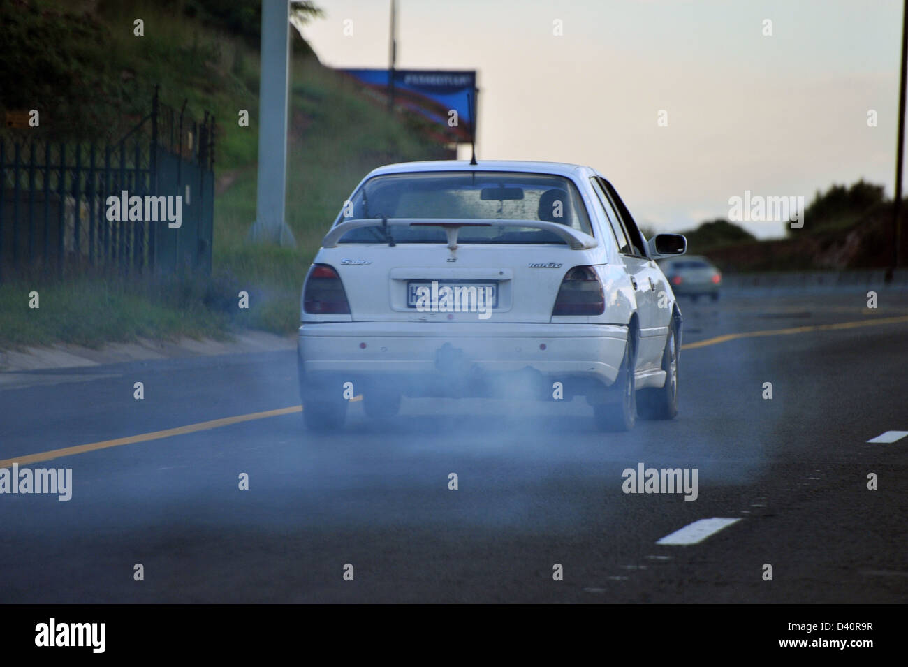 A broken car driving along the motorway with a plume of smoke behind it ...