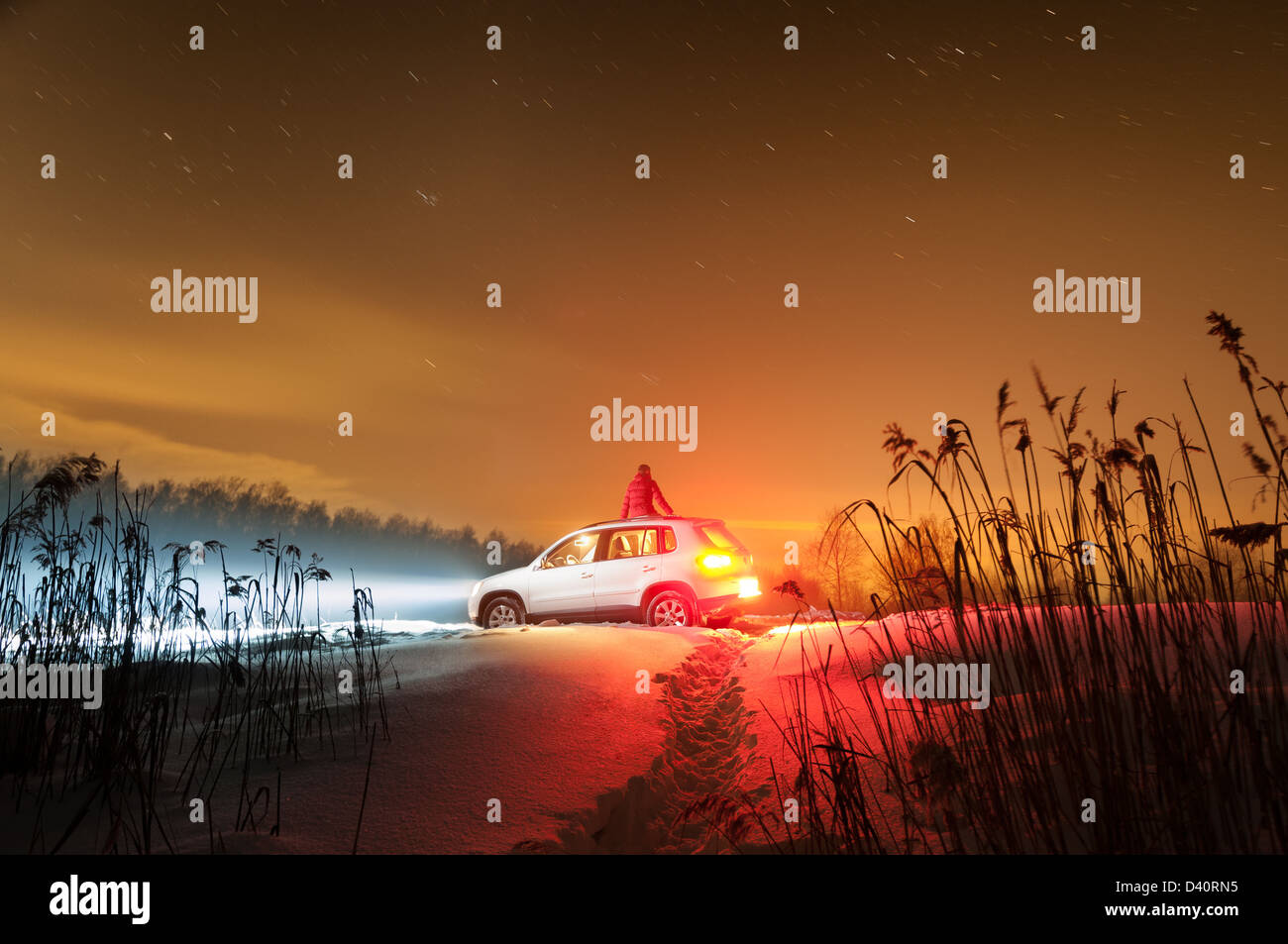 Starry winter night. White car with woman sitting on it. Headlights ...