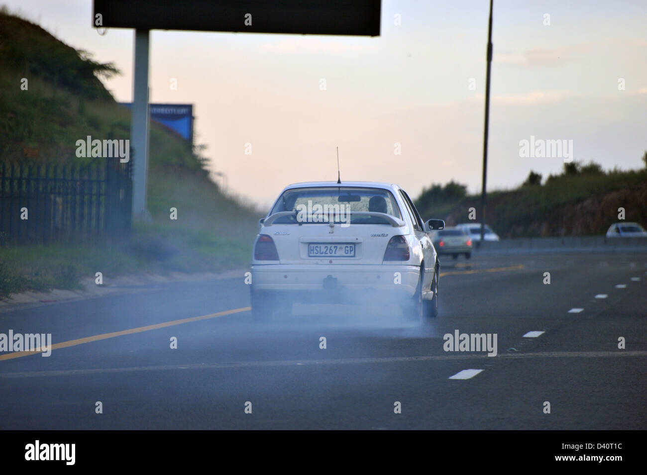 A broken car driving along the motorway with a plume of smoke behind it ...