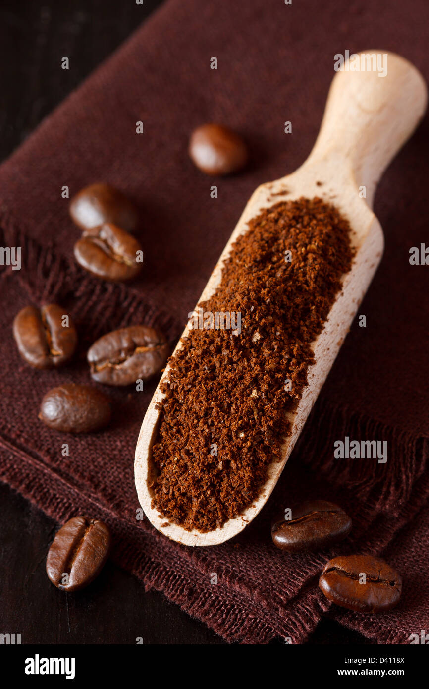Fresh ground coffee in a wooden scoop and coffee beans on a brown ...
