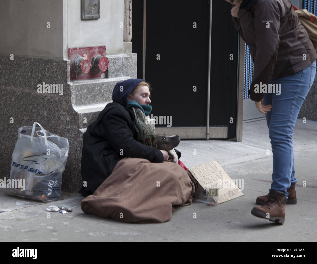 Homeless woman with her dog on the street. Her sign reads, "everyone ...