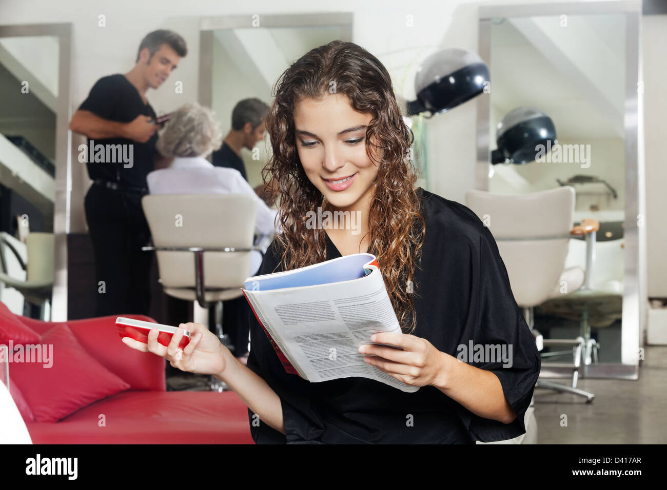 Woman With Mobile Phone Reading Magazine At Hair Salon Stock Photo - Alamy