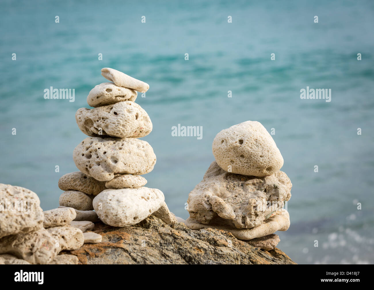 Multiple stacks of pebbles on rock by sea shore with sun lighting the ...