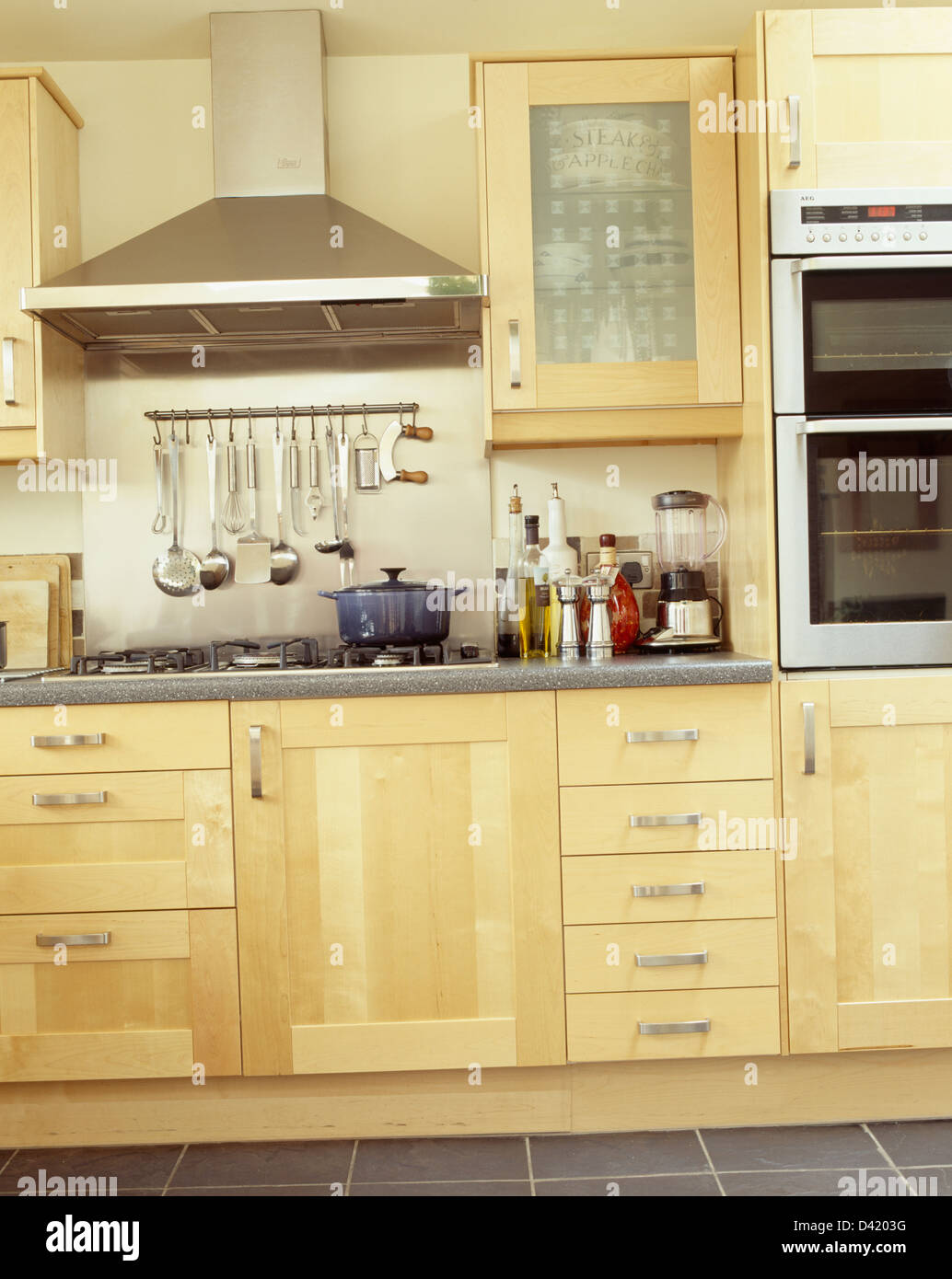 Extractor fan and rack with stainless steel utensils above built-in hob ...