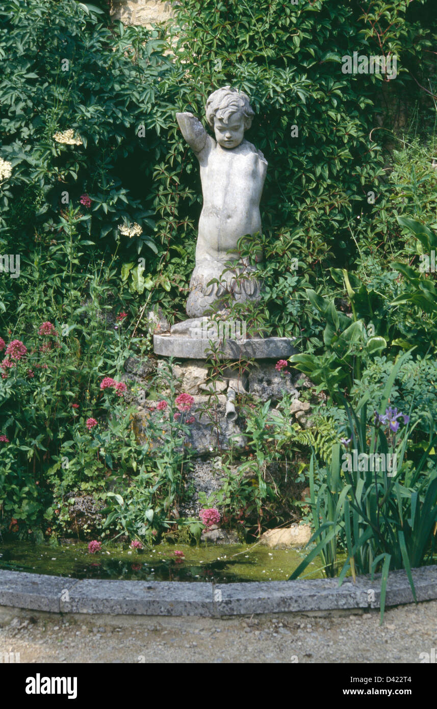 Stone statue of cherub on plinth above small garden pool Stock Photo ...