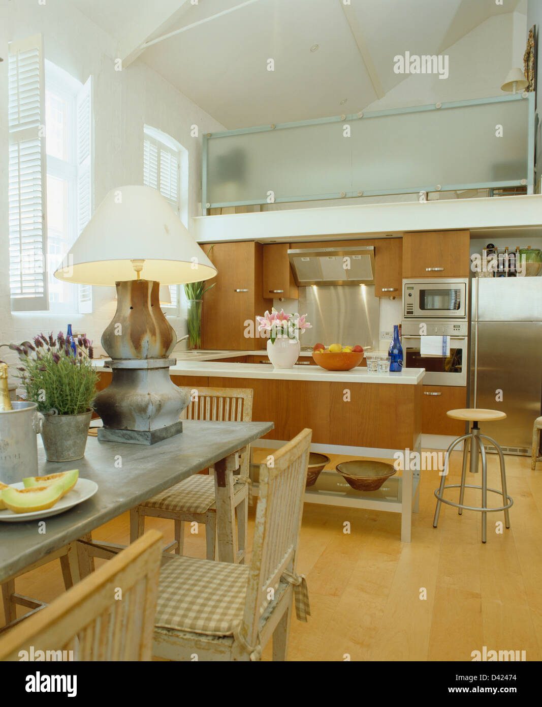 Lighted lamp on zinc-topped table with wooden chairs in modern kitchen ...