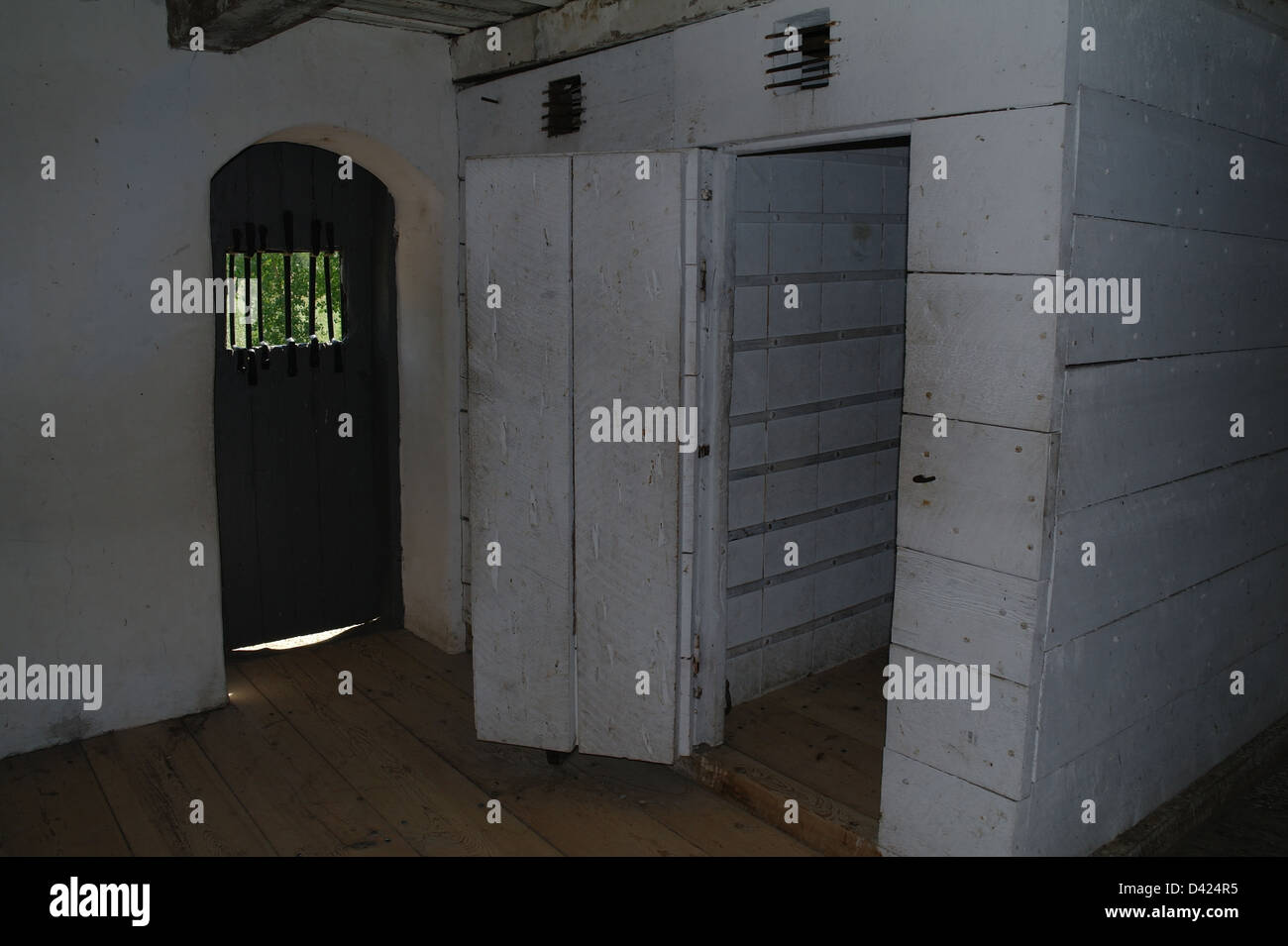 Dark building interior view barred entry door, 2 narrow white painted ...