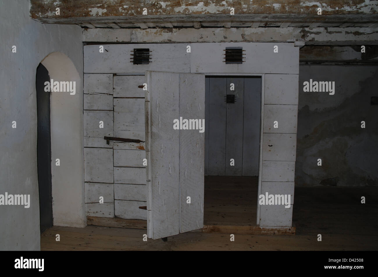 Two small narrow white painted prison cells (1 door open), dark ...