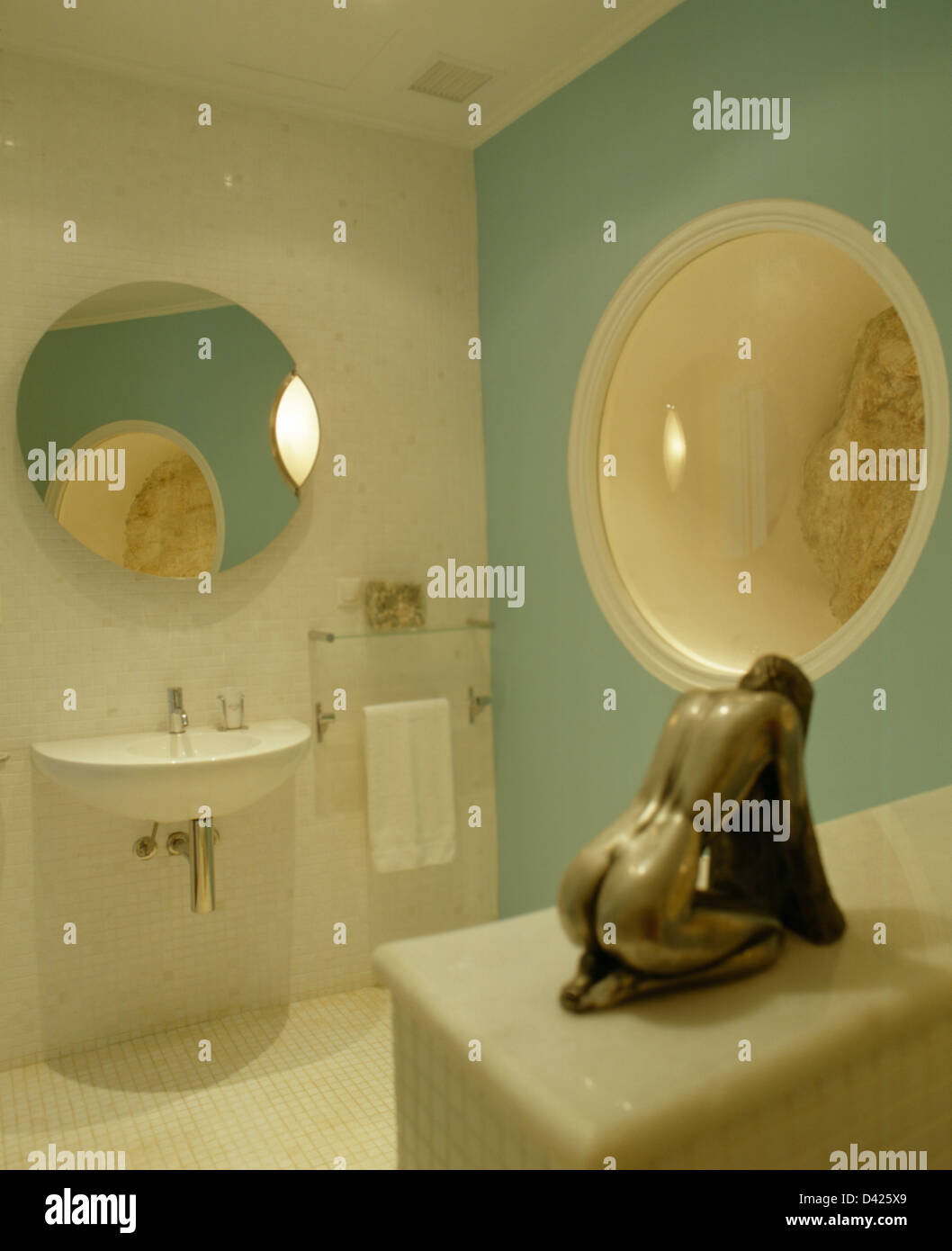 Bronze statue in modern pastel turquoise bathroom with circular mirror ...