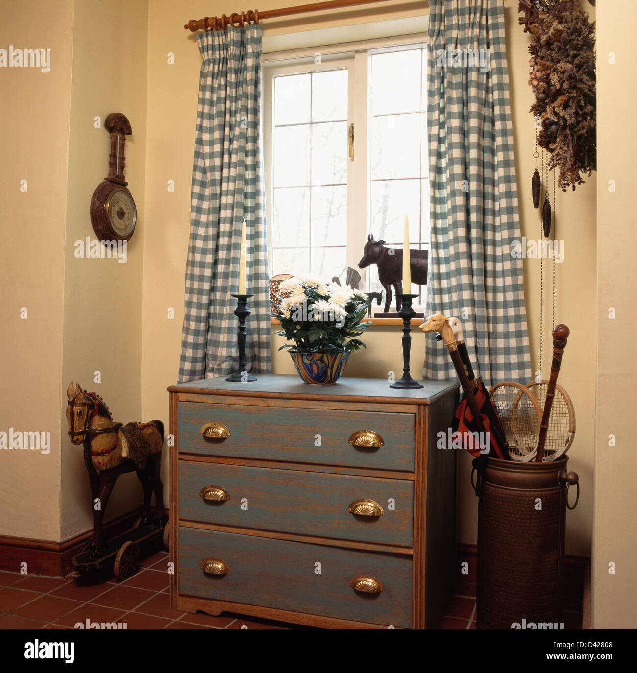 Blue checked curtains on window above blue chest of drawers with ...