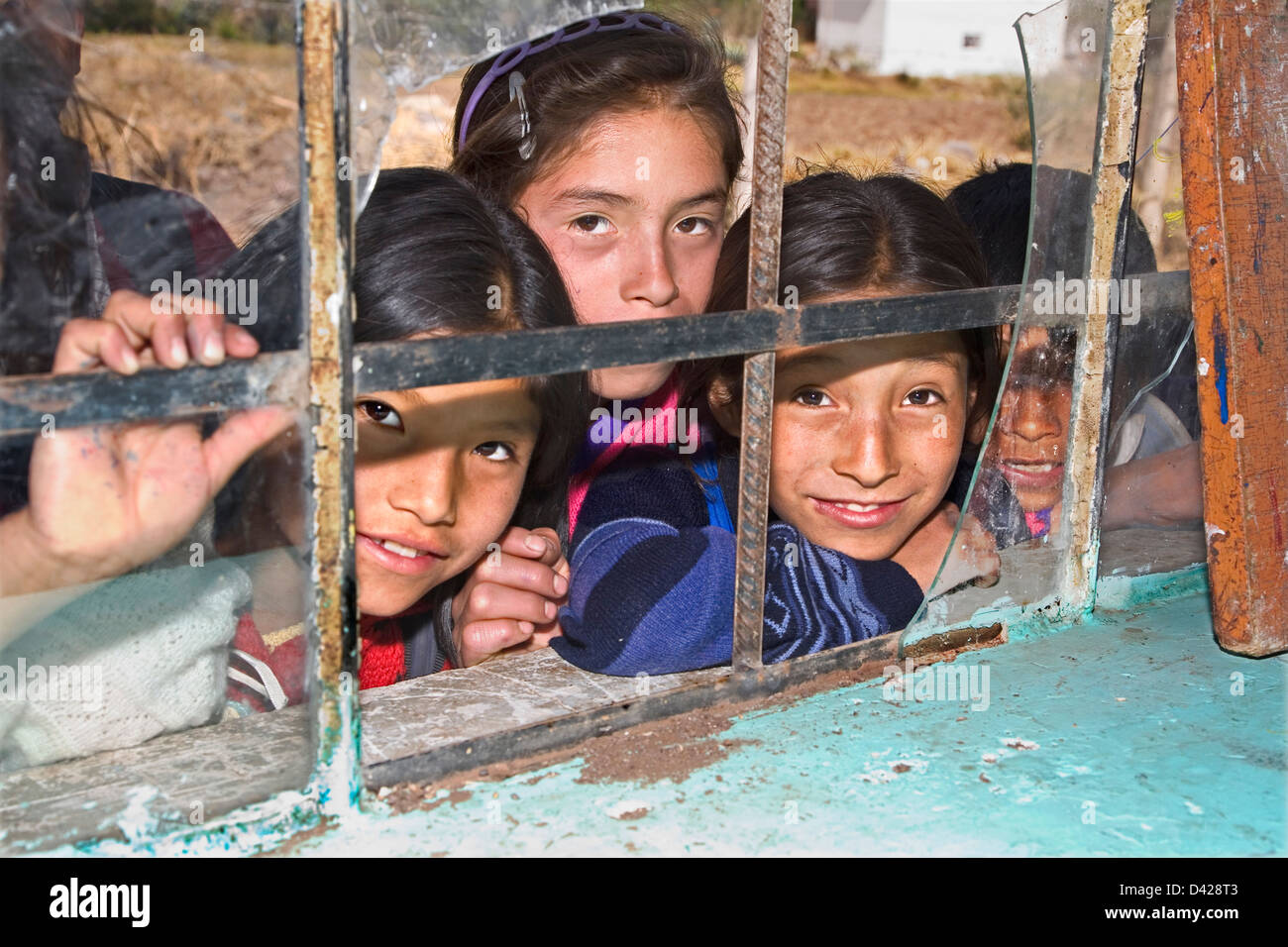 Three smiling girls and one boy peak through broken window from ...