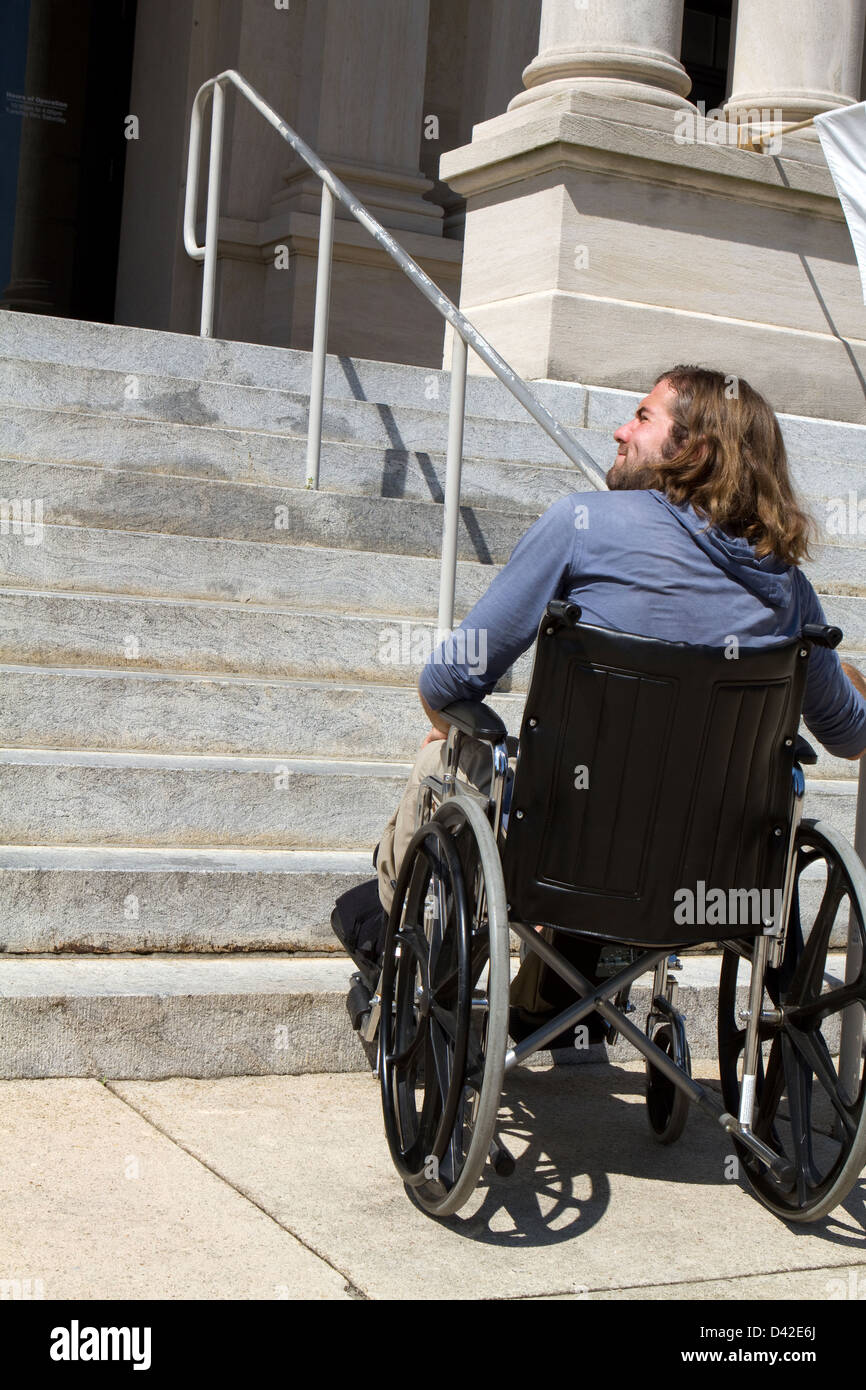Disabled man in wheelchair looks for a ramp to gain access to a public ...