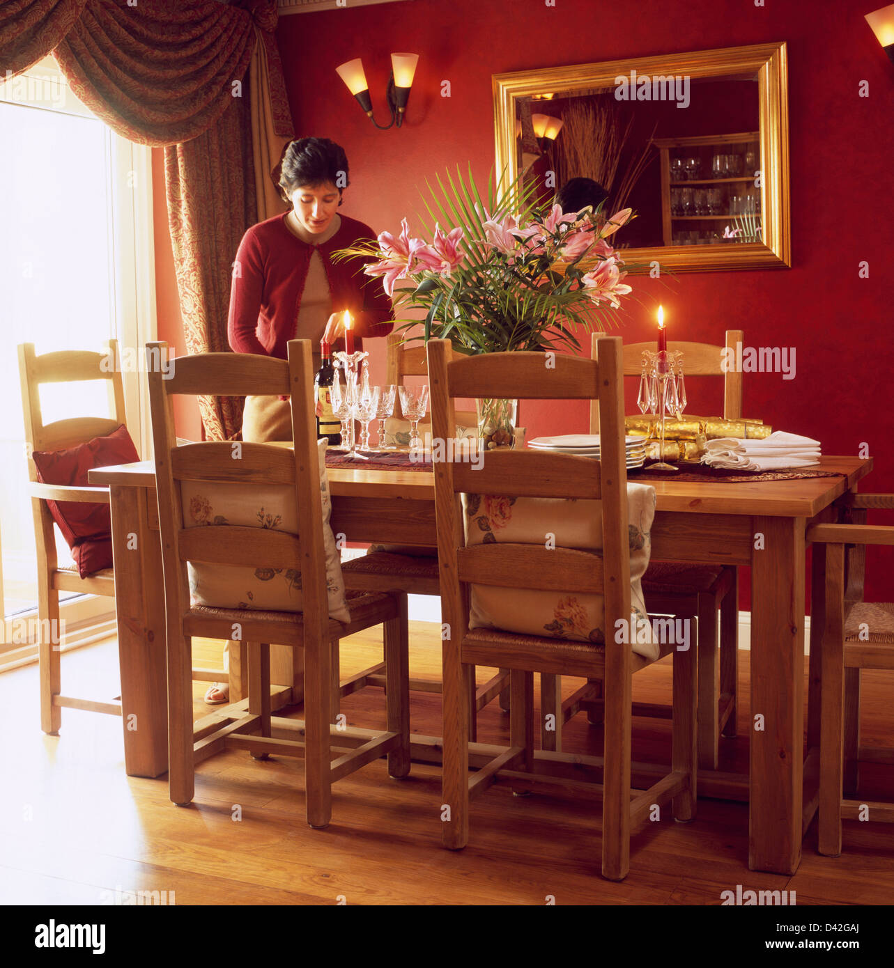 Woman setting table with lighted candles for dinner in red dining room ...