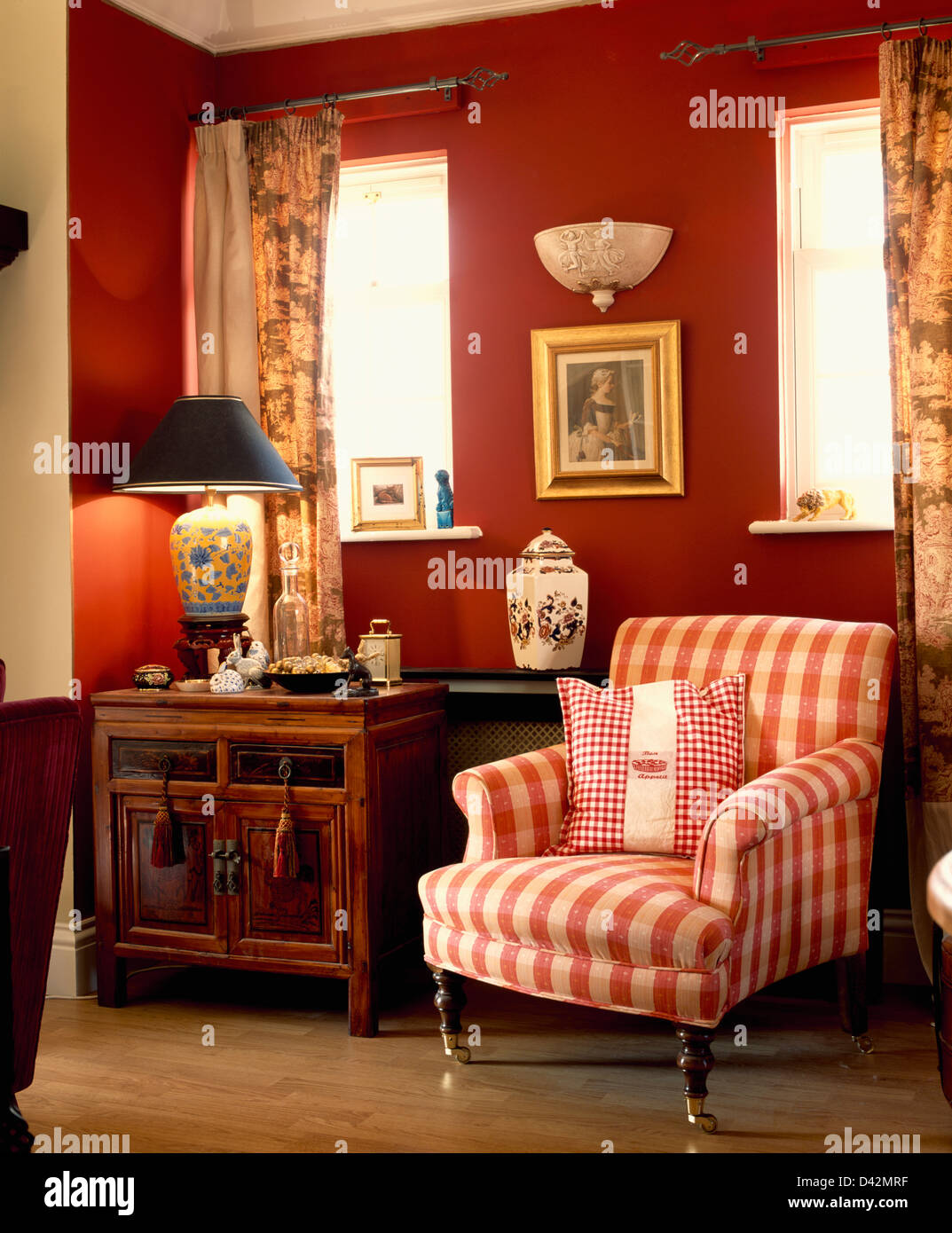 Red checked armchair beside wooden chest with lighted lamp in corner of ...