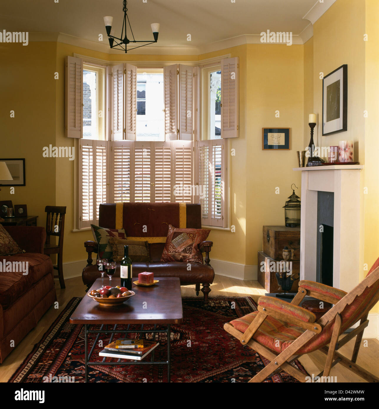 Small brown leather sofa below window with plantation shutters in ...