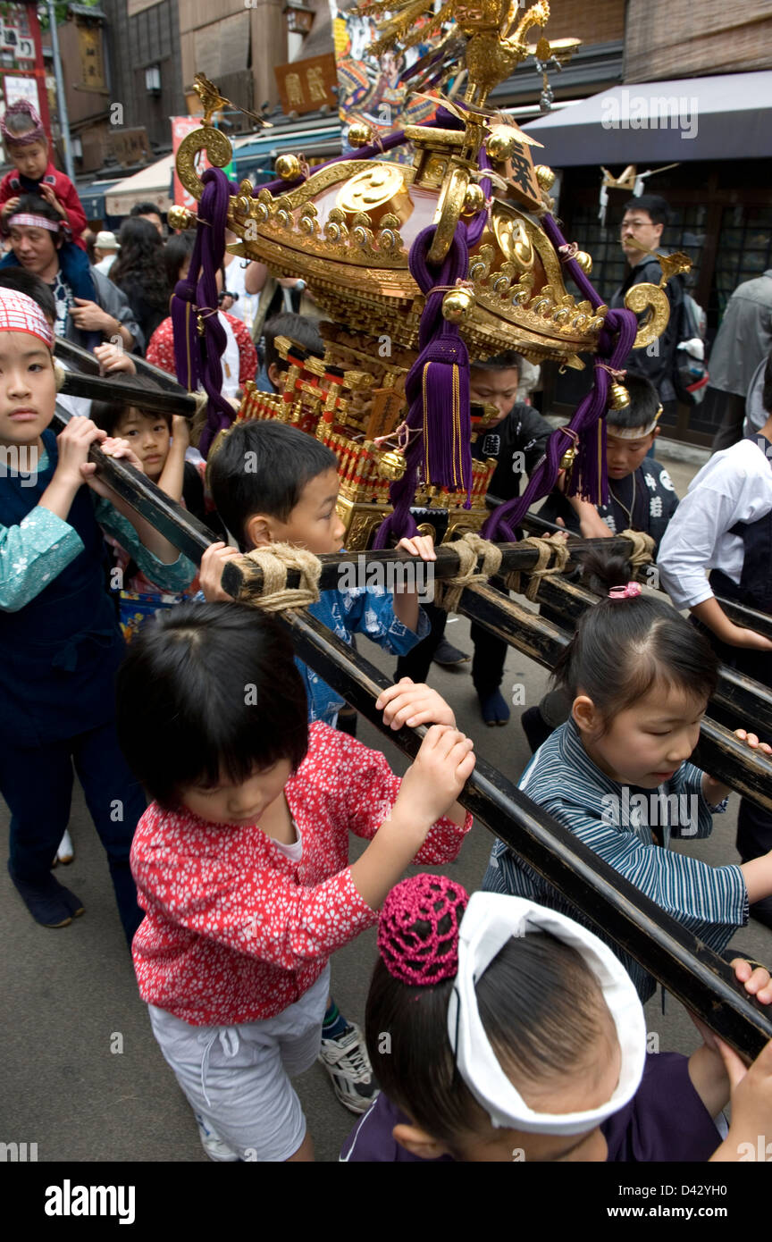Boys and girls carry a gold decorated sacred mikoshi portable shrine in ...