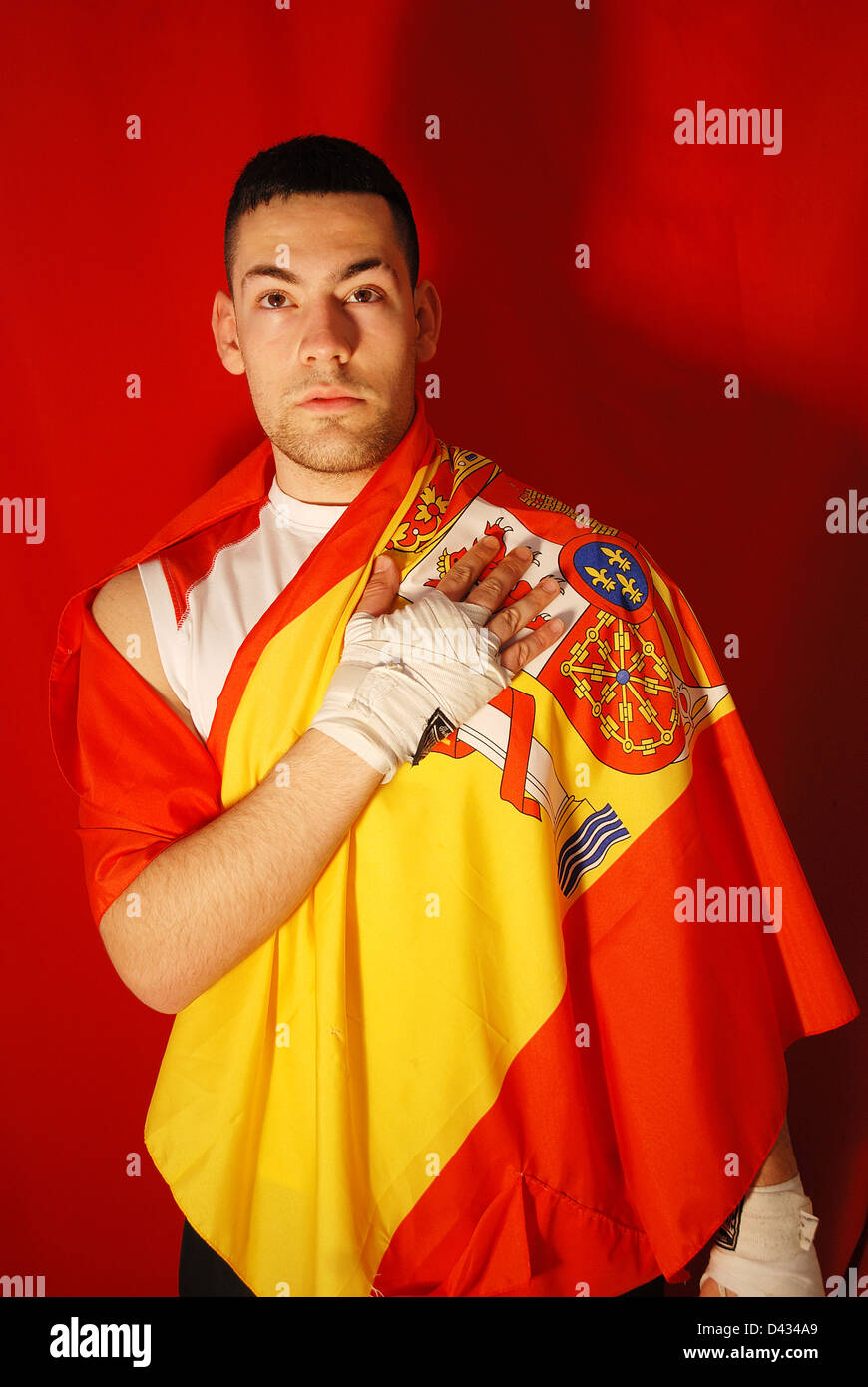 Young man wrapped in a Spanish flag, hand on heart and looking up Stock ...