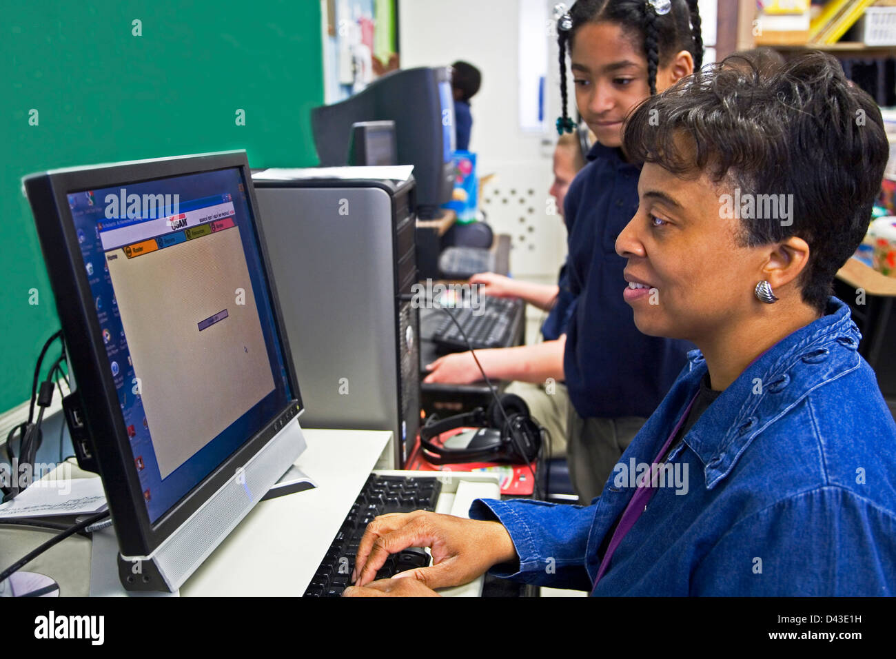African American female teacher instructs young girl on computer in ...
