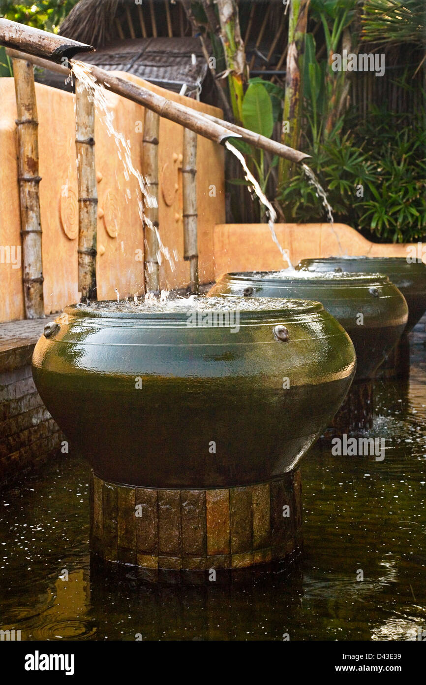 Water falls from three bamboo poles into three pottery urns in fountain ...