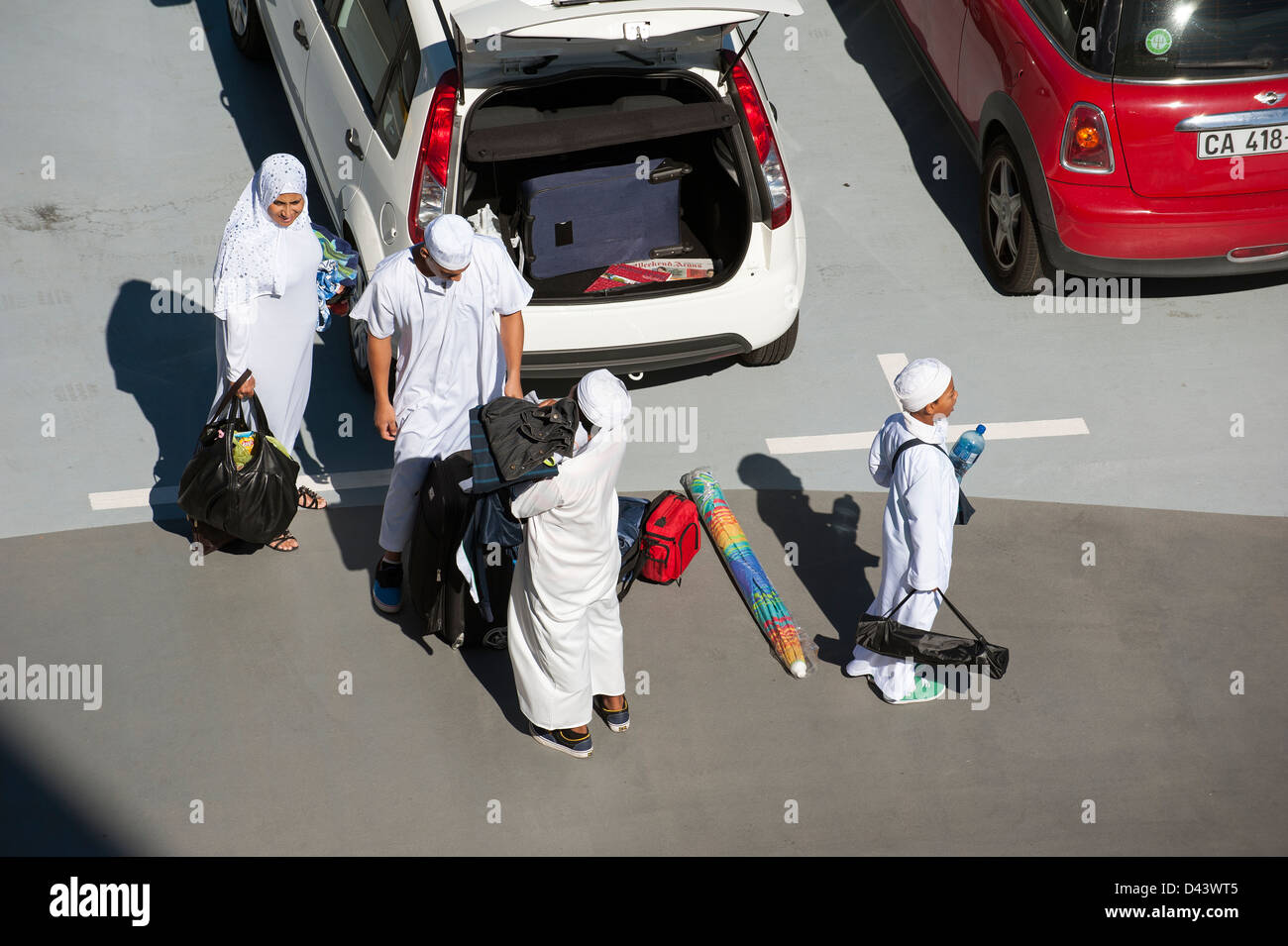 Muslim family wearing traditional white clothing packing the boot of a ...