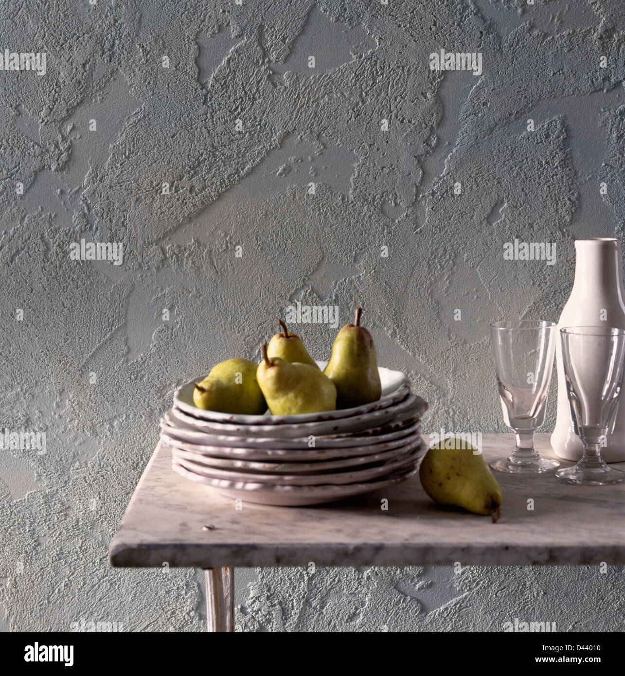 Close-up of pears on stack of white pottery bowls on marble table in front of textured plastered ...