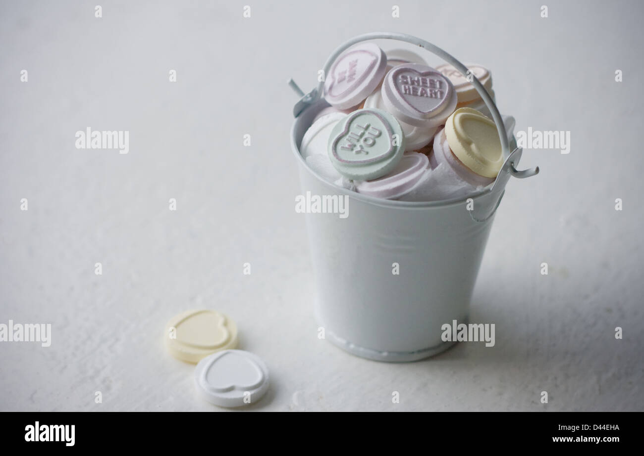 A little bucket of love heart sweets on a white surface Stock Photo - Alamy